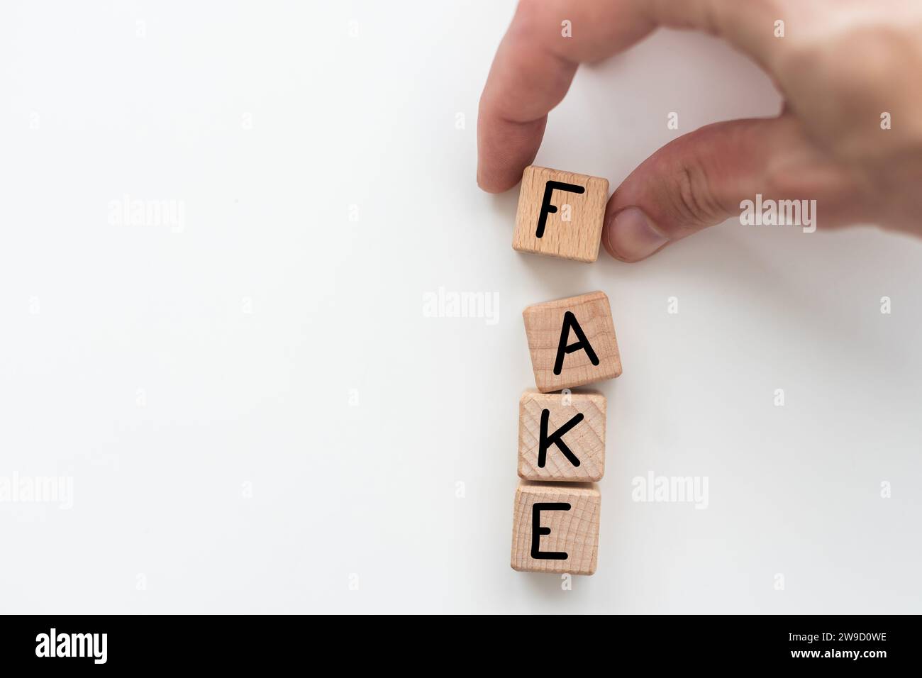 The word FAKE, spelt with wooden letter tiles, over a white background ...