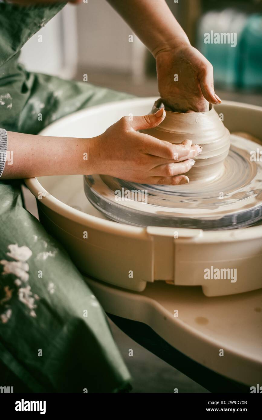 Female hands moulding the walls of a clay ware on potters wheel Close ...