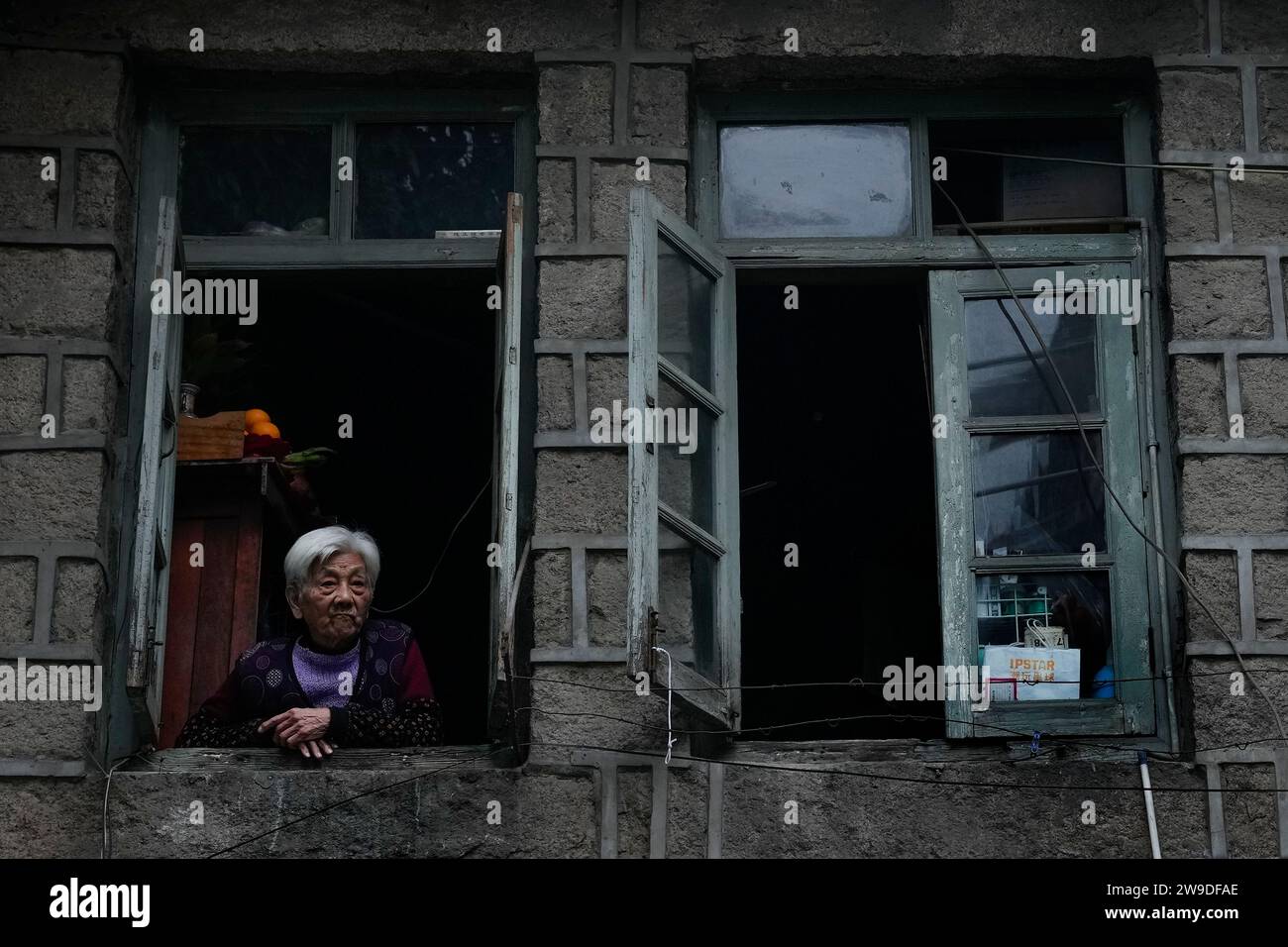 An elderly woman looks out from her room window at an old shop houses ...