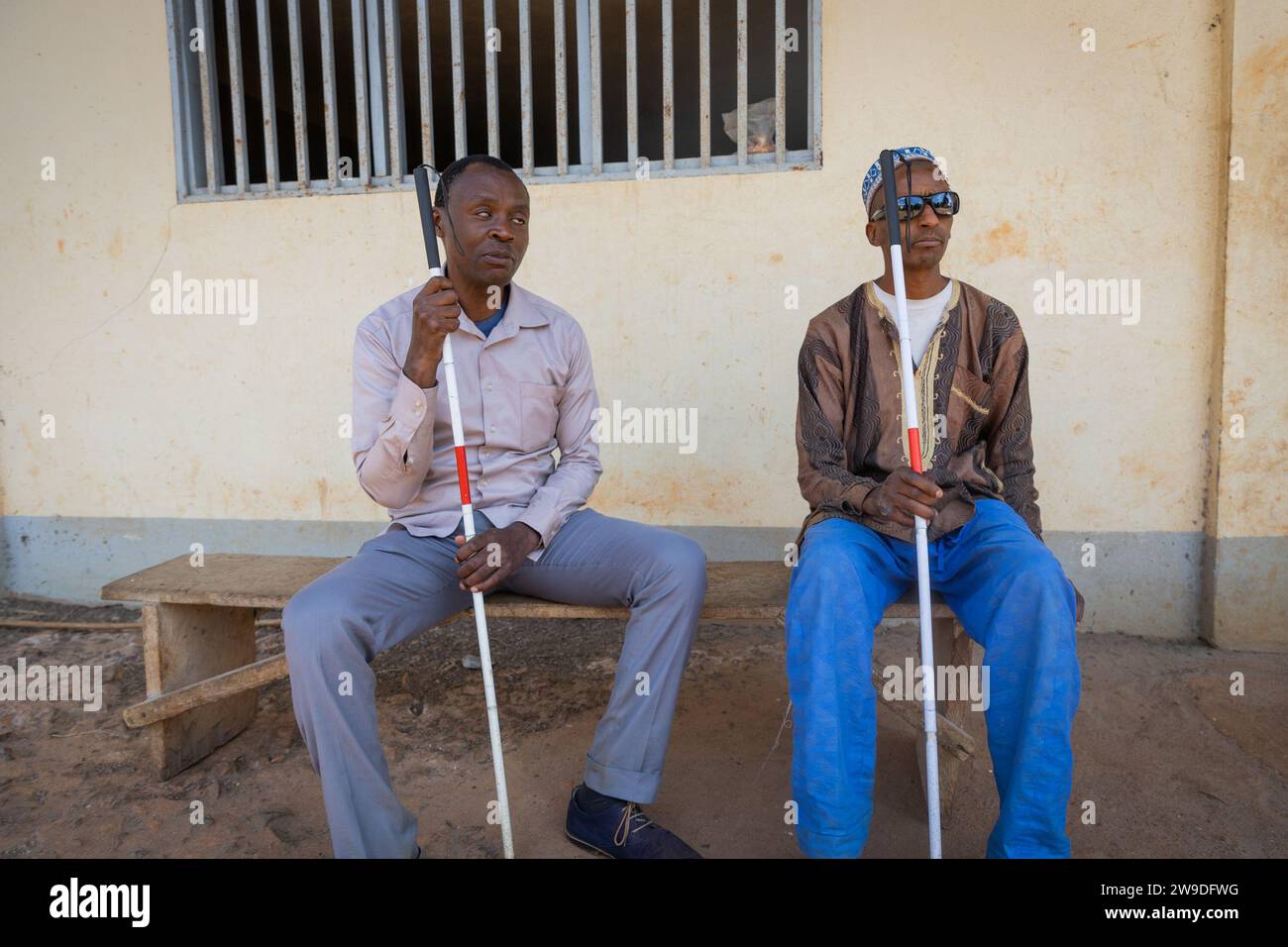 Two blind friends rest sitting on a wooden platform holding their white ...