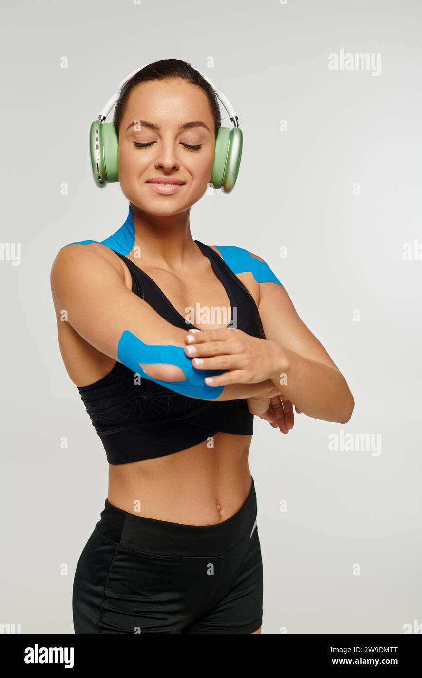 attractive jolly woman in sport wear with headphones and kinesiological ...