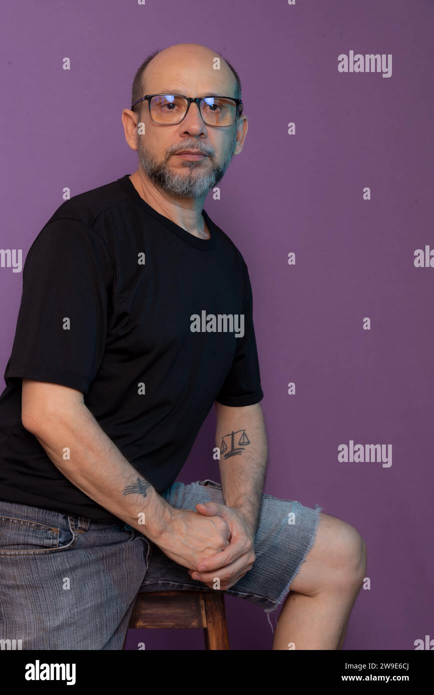 Bearded Bald White Man Wearing Prescription Glasses Sitting On Wooden