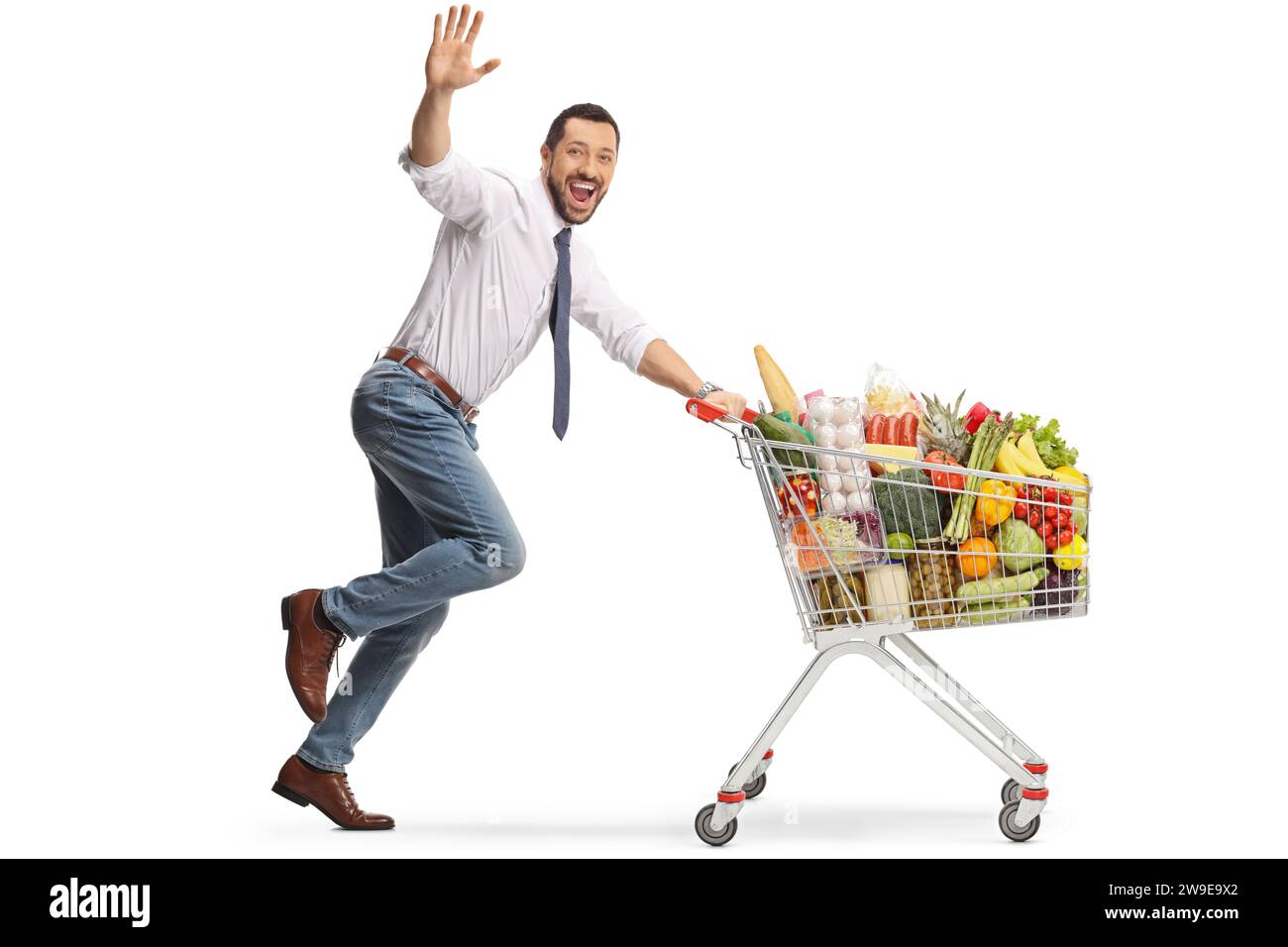 Cheerful man running with food in a shopping cart and waving at camera ...