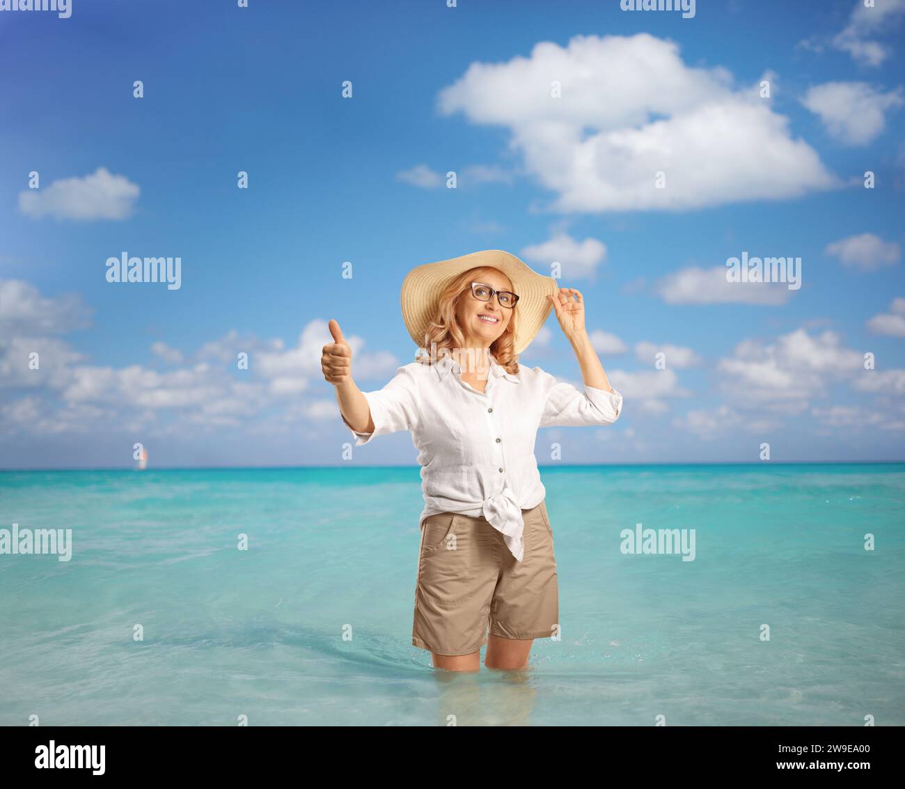 Middle aged woman with a straw hat dipping in the sea and gesturing ...