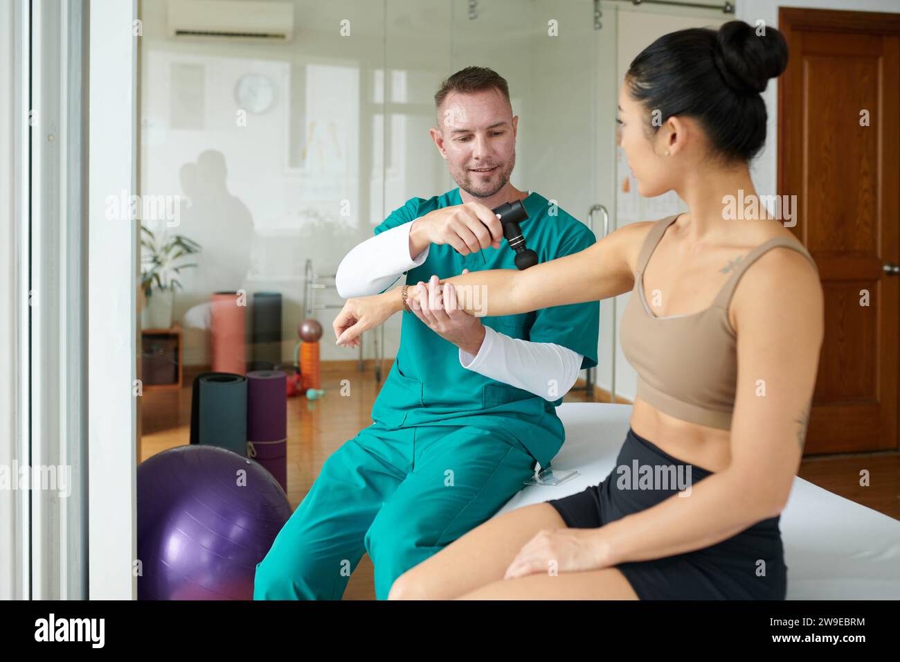 Therapist using massage gun when working on tense arm muscles of ...