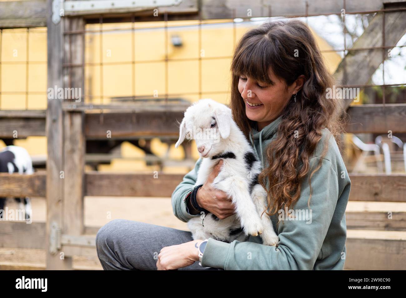 Happy young farmer woman hugging a baby goat on a rural organic farm ...