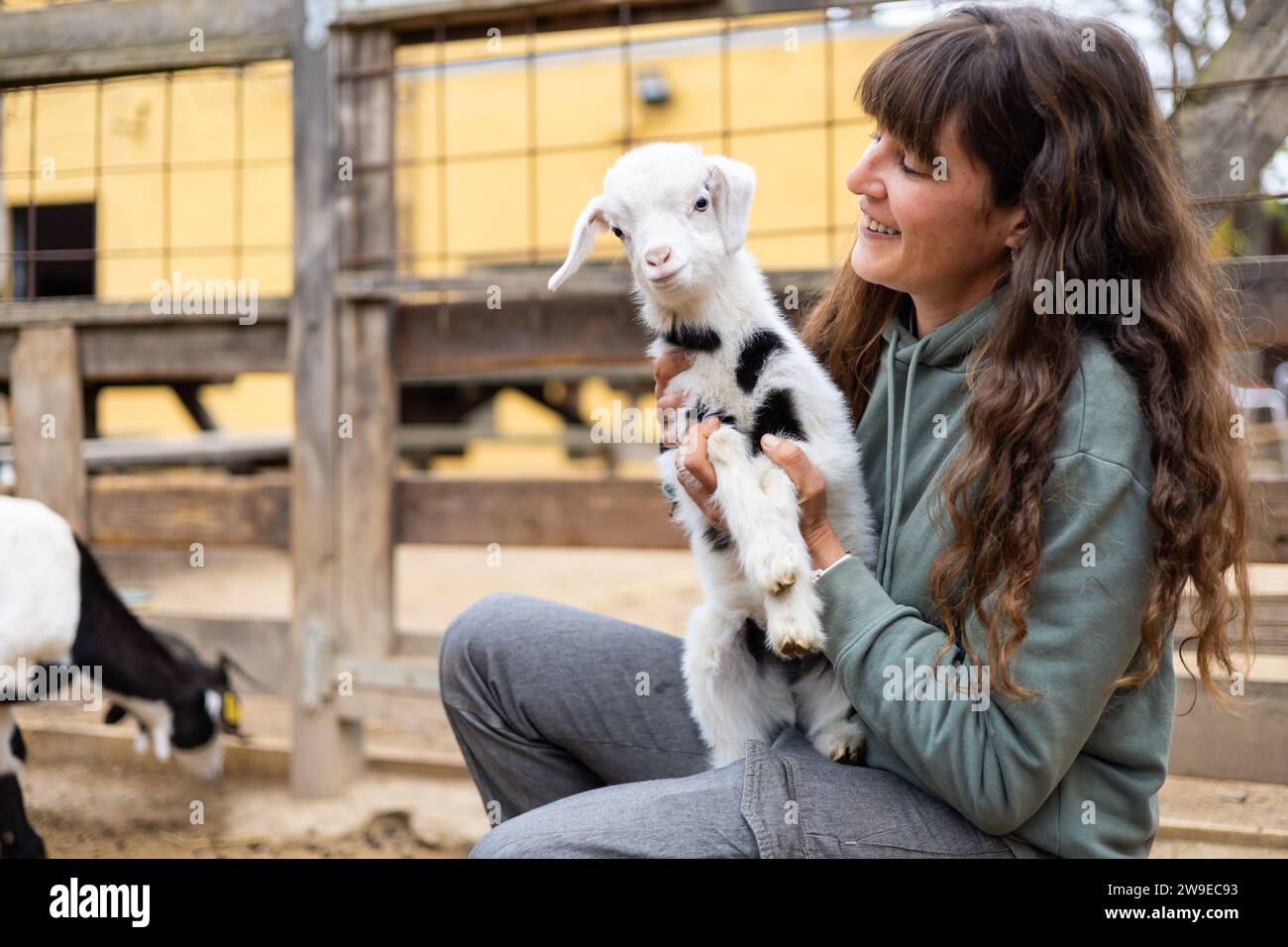 Happy young farmer woman hugging a baby goat on a rural organic farm ...
