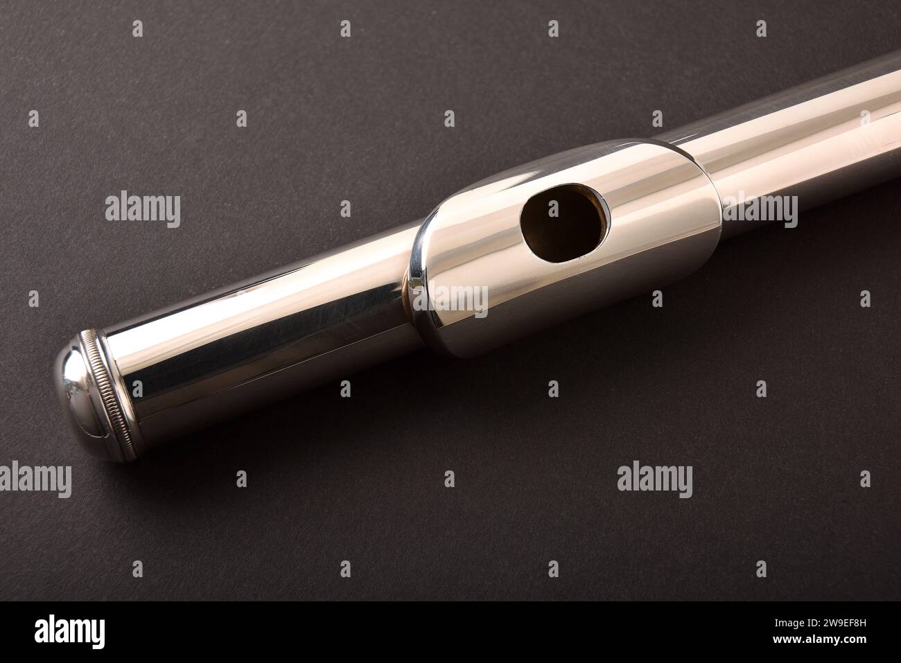 Detail of the head of a metal flute on black table. Top elevated view ...