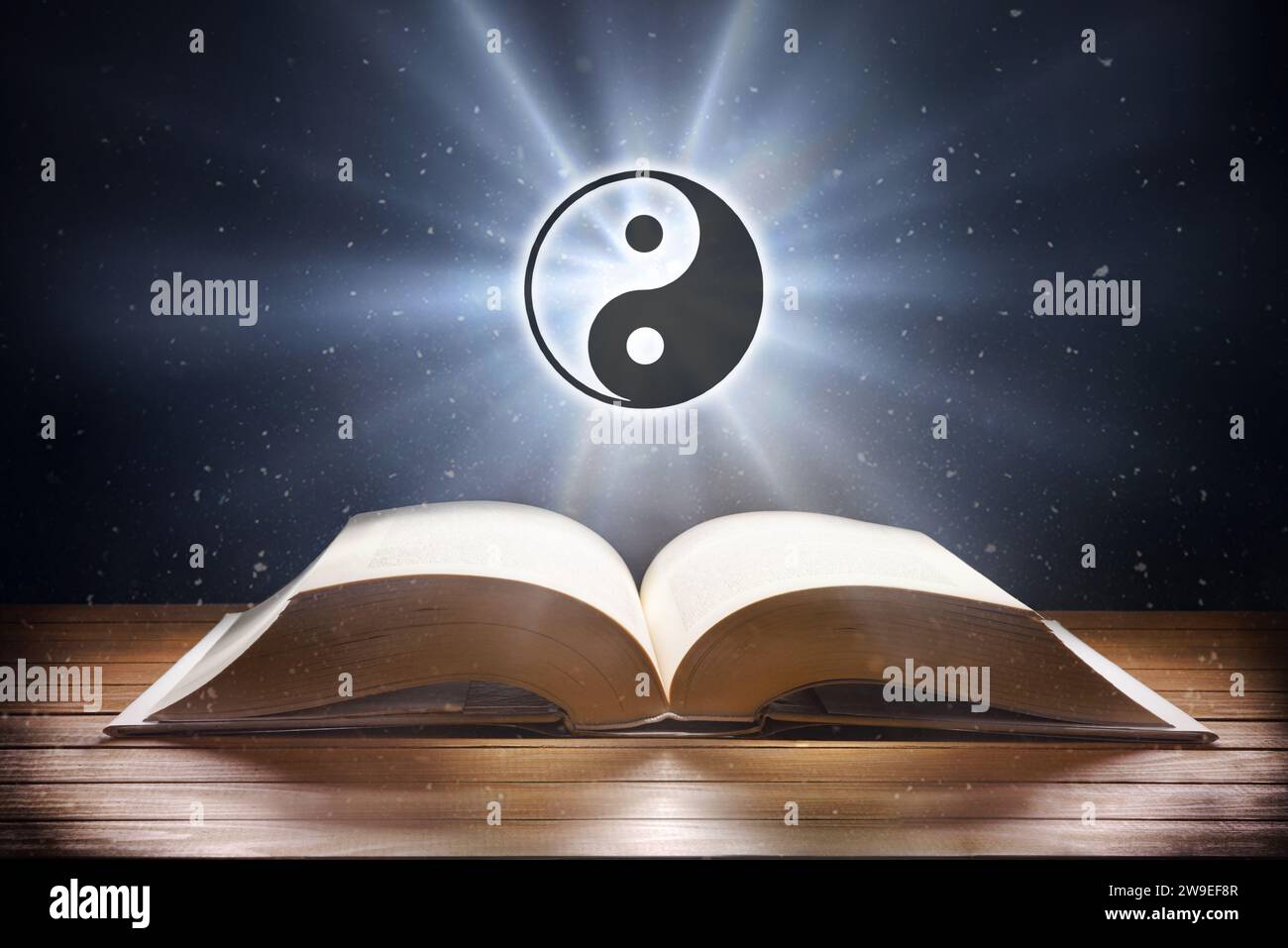 Open book on wooden table and taoist symbol with beam of light with ...