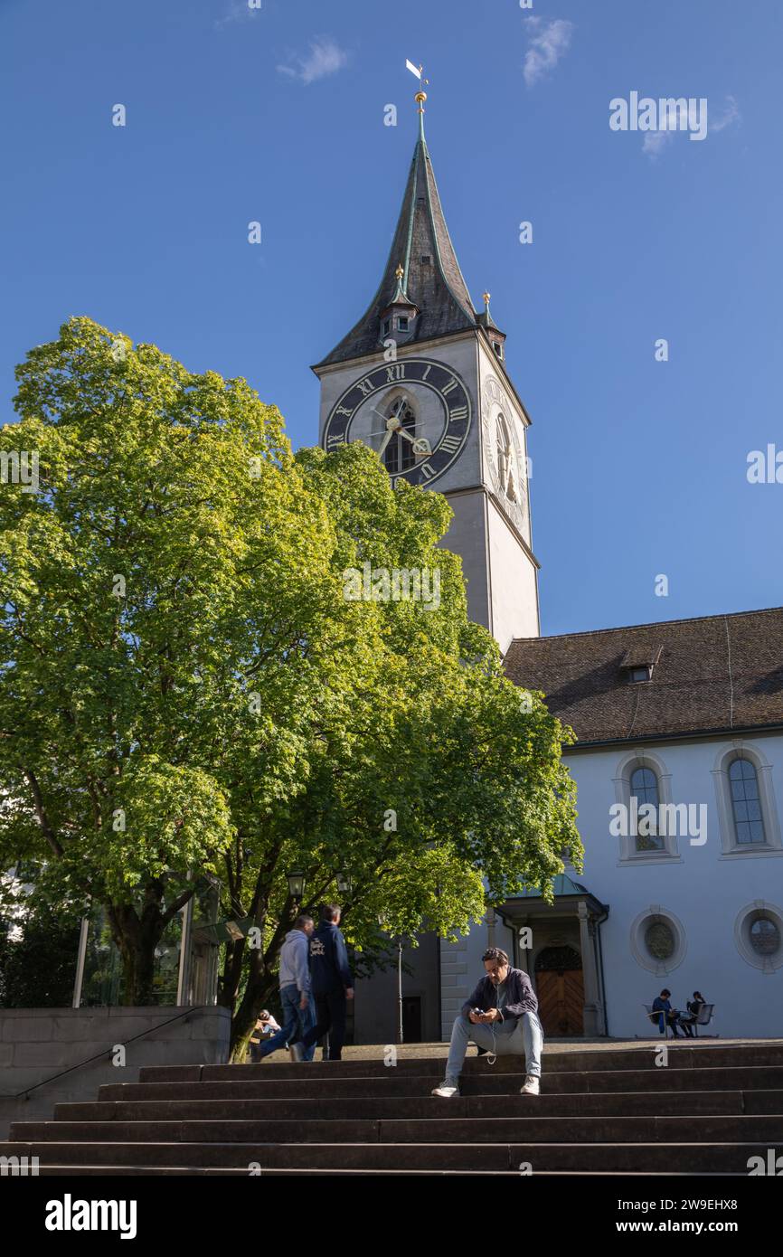 Man sitting on the steps of the St. Peter Church in old town Zurich ...