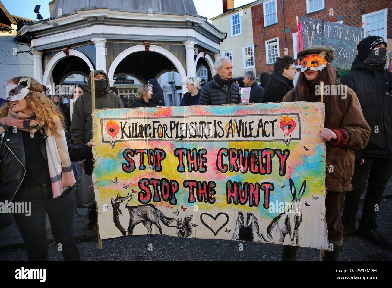Protesters, some wearing animal face masks stand behind a banner saying ...