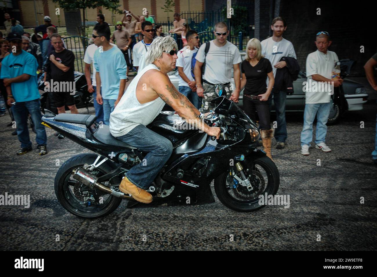 A man rides a powerful motorbike without a helmet as a crowd of people ...