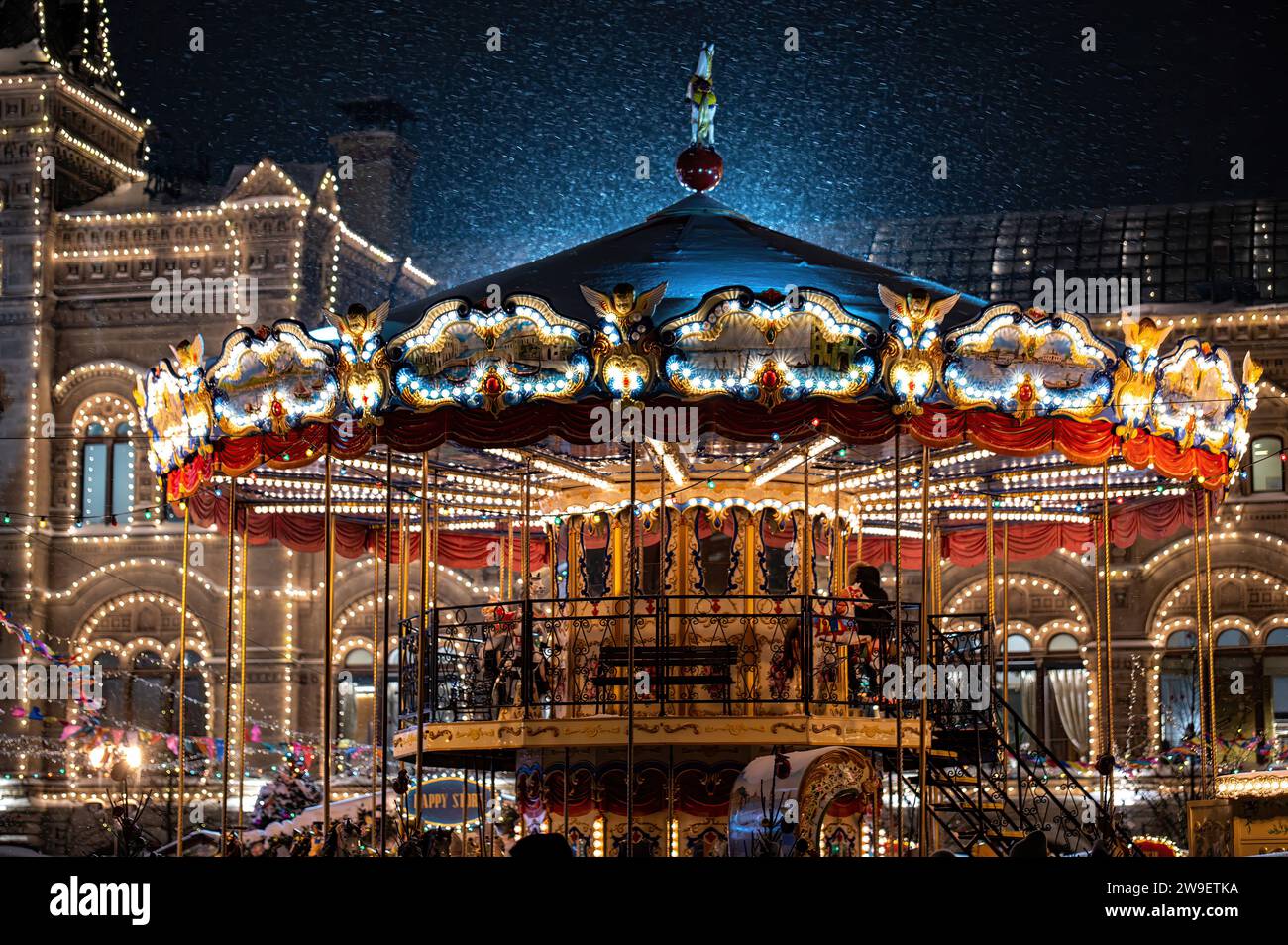 beautiful bright carousel in park at night in winter. Snowfall in rim ...