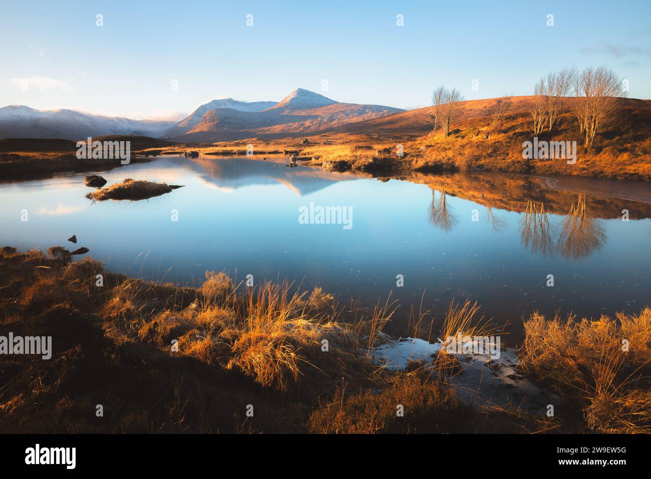 Gold light cast across a calm, tarn reflection and moorland at Rannoch ...