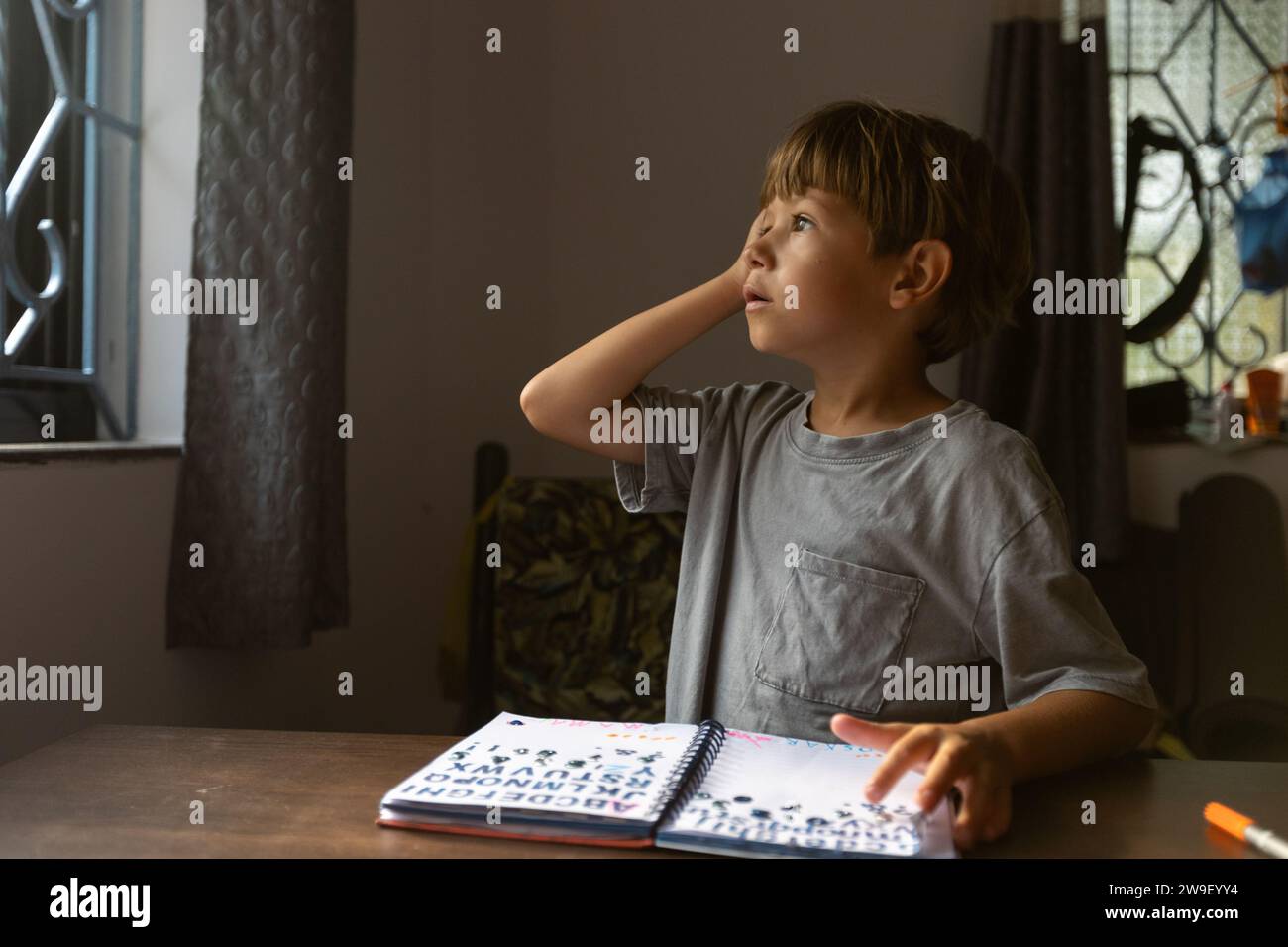Preschooler boy sits at table near window and learns letters that are ...