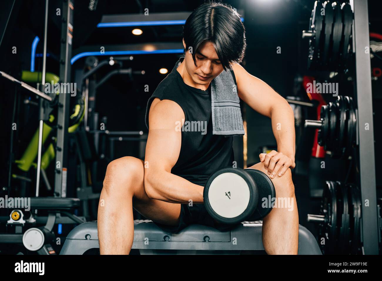 handsome young Asian man sitting on an exercise bench holding a heavy ...