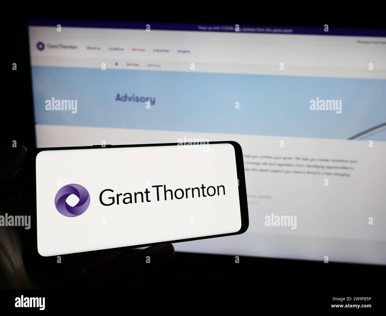 Person holding mobile phone with logo of consulting company Grant ...