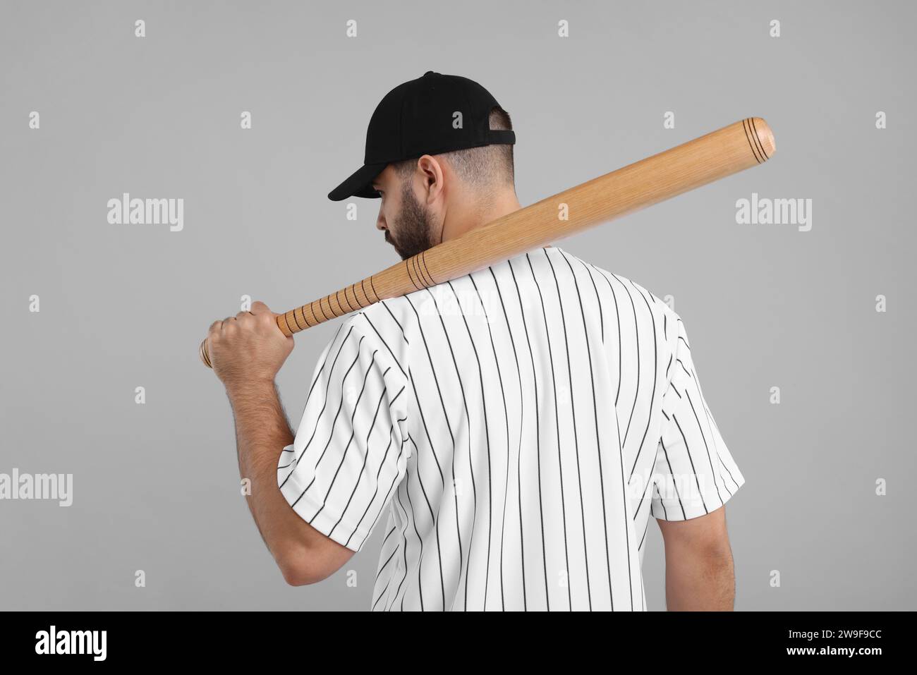 Man in stylish black baseball cap holding bat on light grey background ...