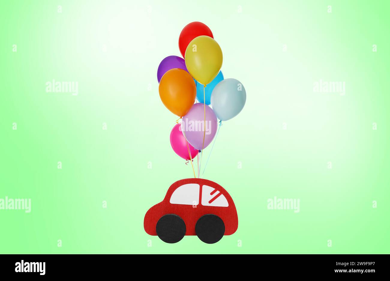 Many balloons tied to toy car flying on light green background Stock ...