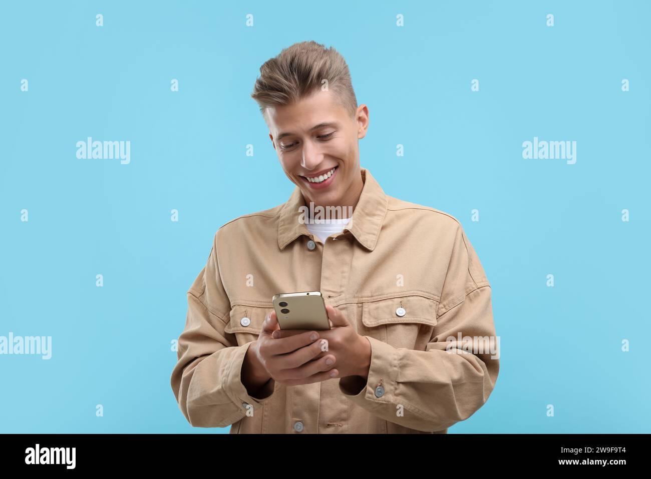 Happy young man sending message via smartphone on light blue background ...