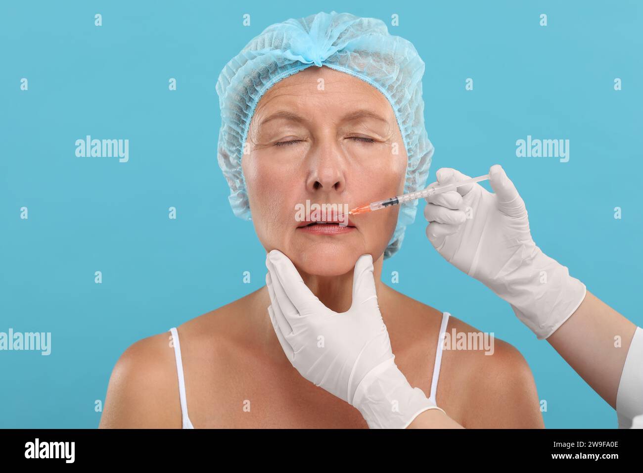 Doctor giving lips injection to senior woman on light blue background ...