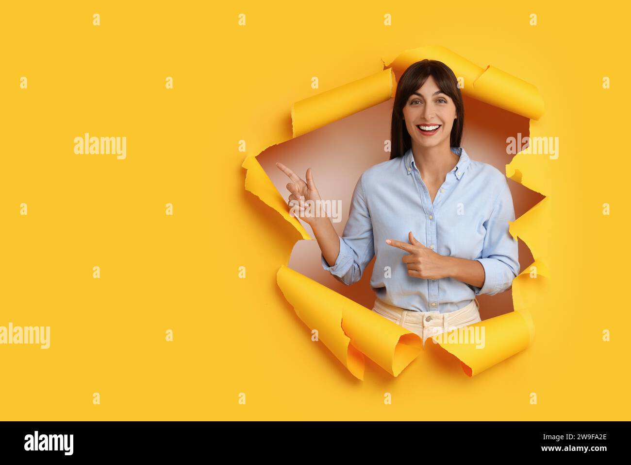 Special promotion. Woman pointing at something through hole in orange ...