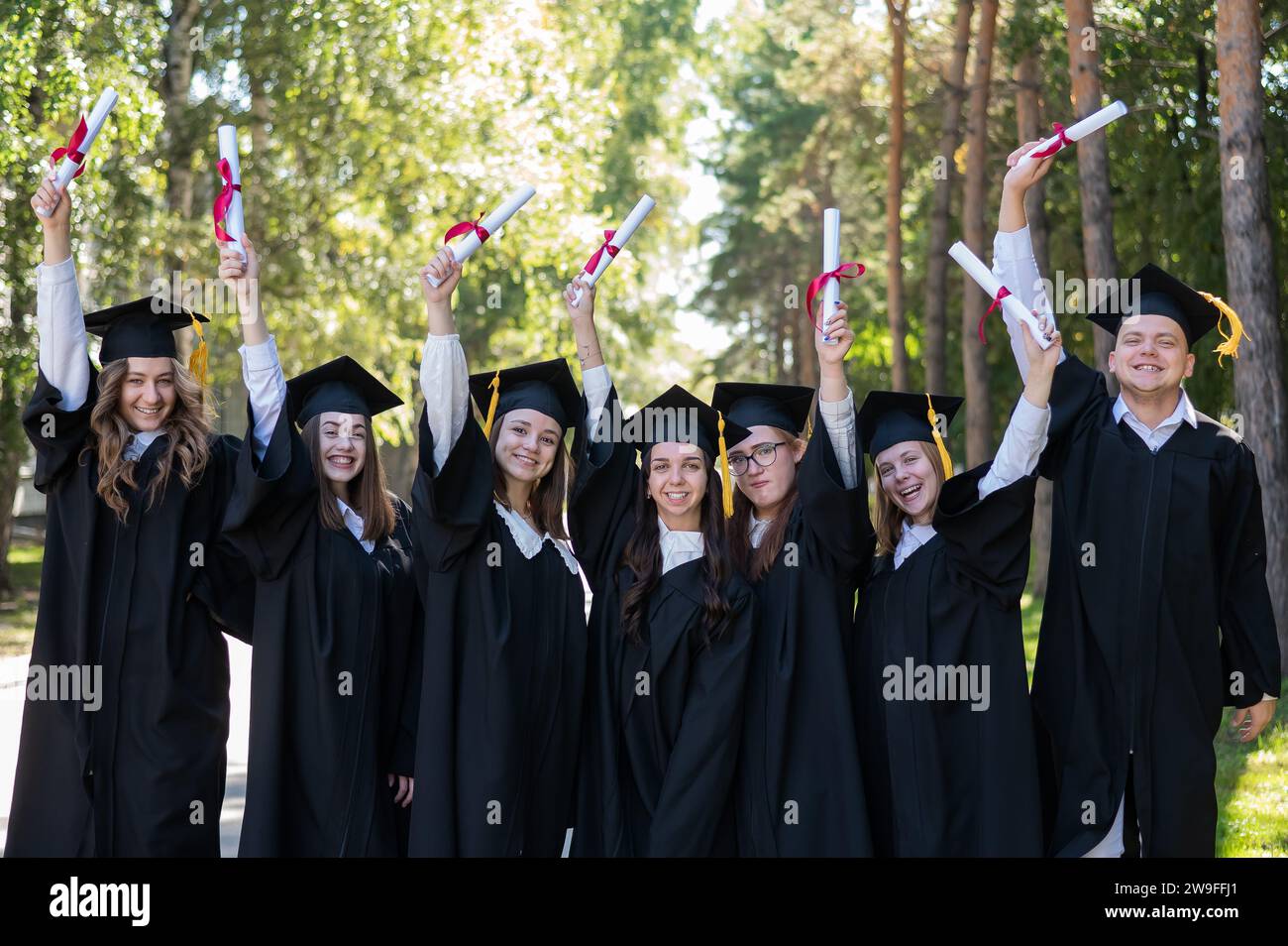 Row of young students in graduation gowns outdoors showing off their ...