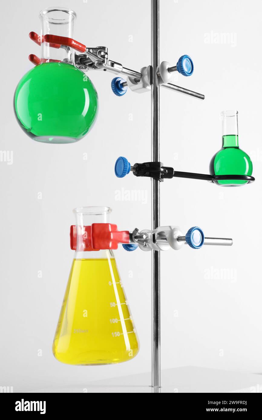 Retort stand and laboratory flasks with liquids on white background ...