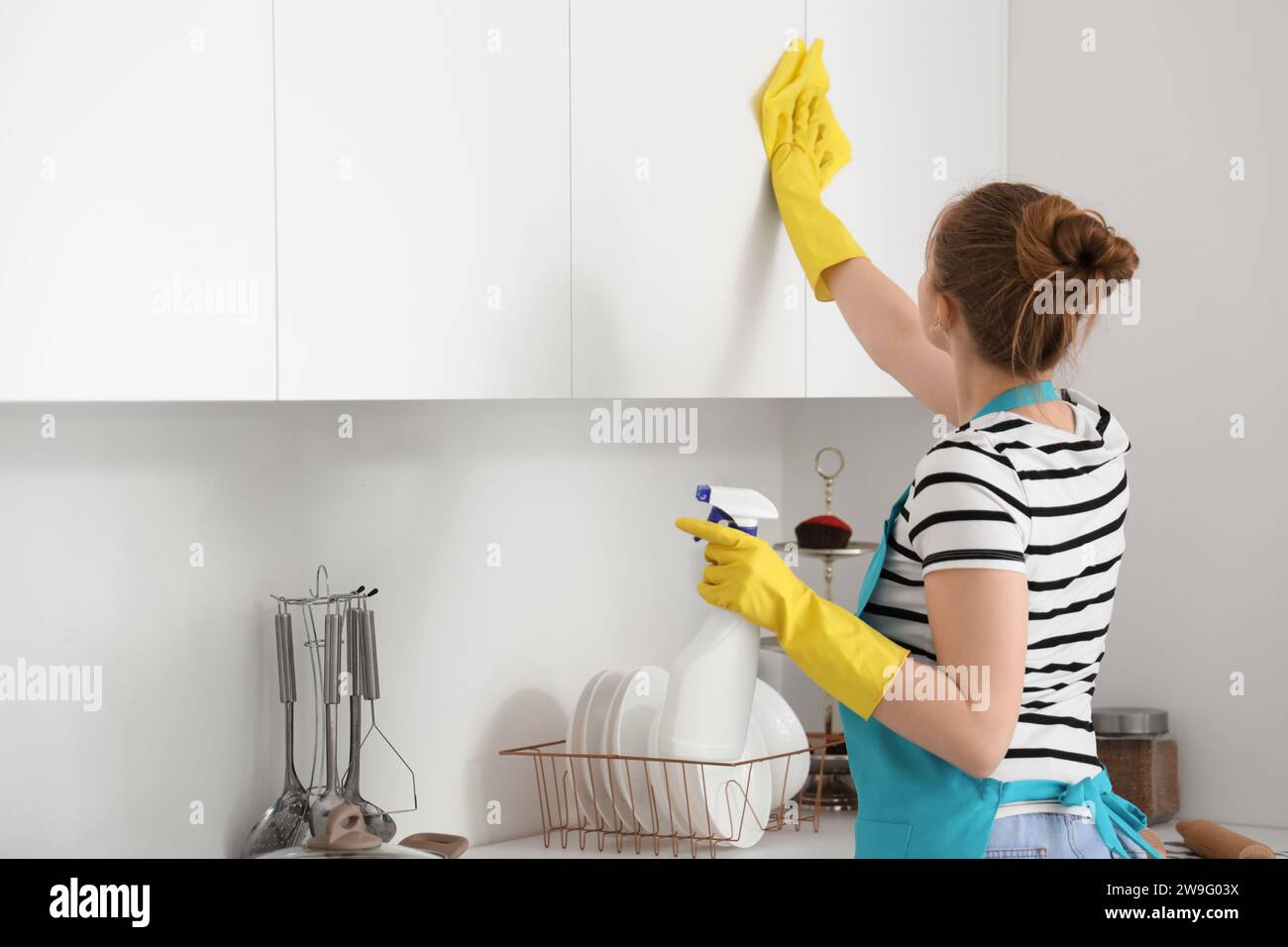 Woman in yellow rubber gloves cleaning cupboards in modern kitchen ...