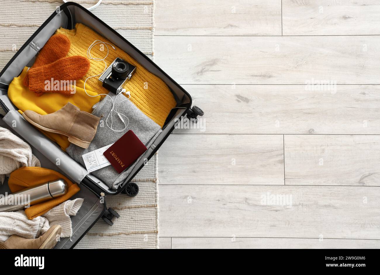 Open suitcase with winter clothes and accessories on carpet, top view ...