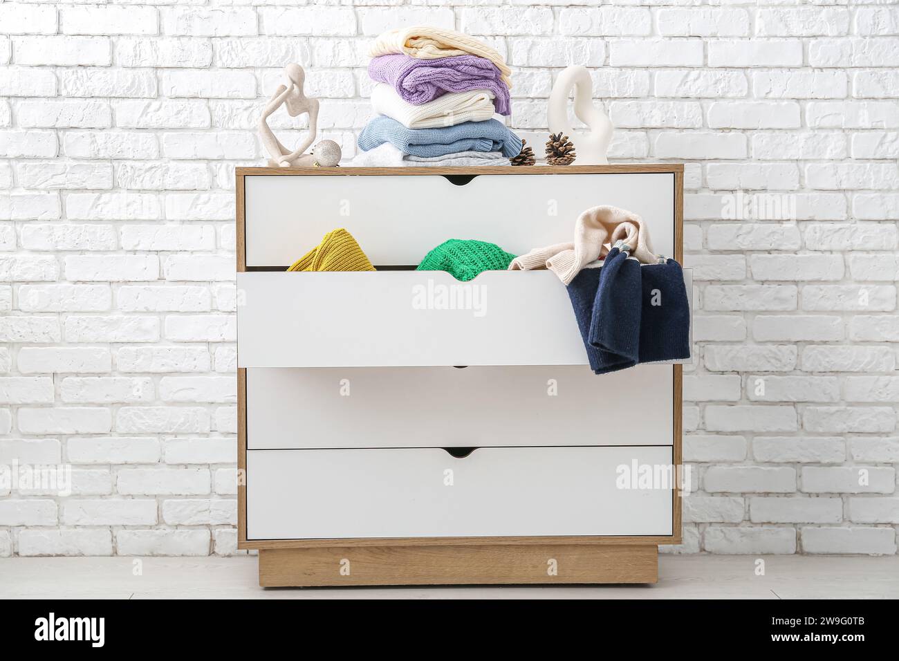 Chest drawers with different stylish sweaters and decor near light ...