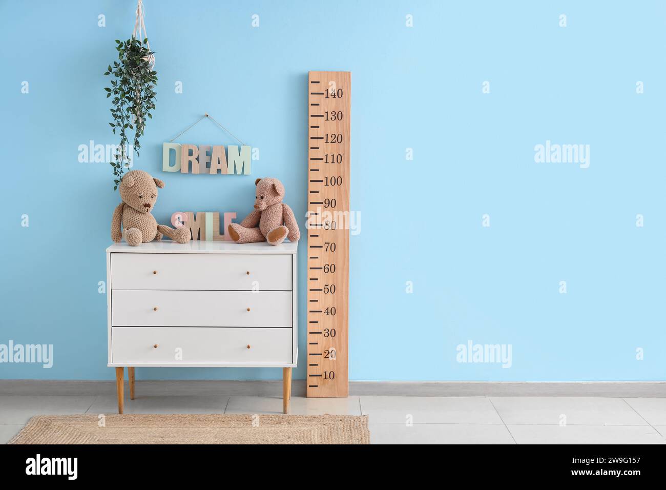 Wooden stadiometer and chest of drawers with plush toys near blue wall ...