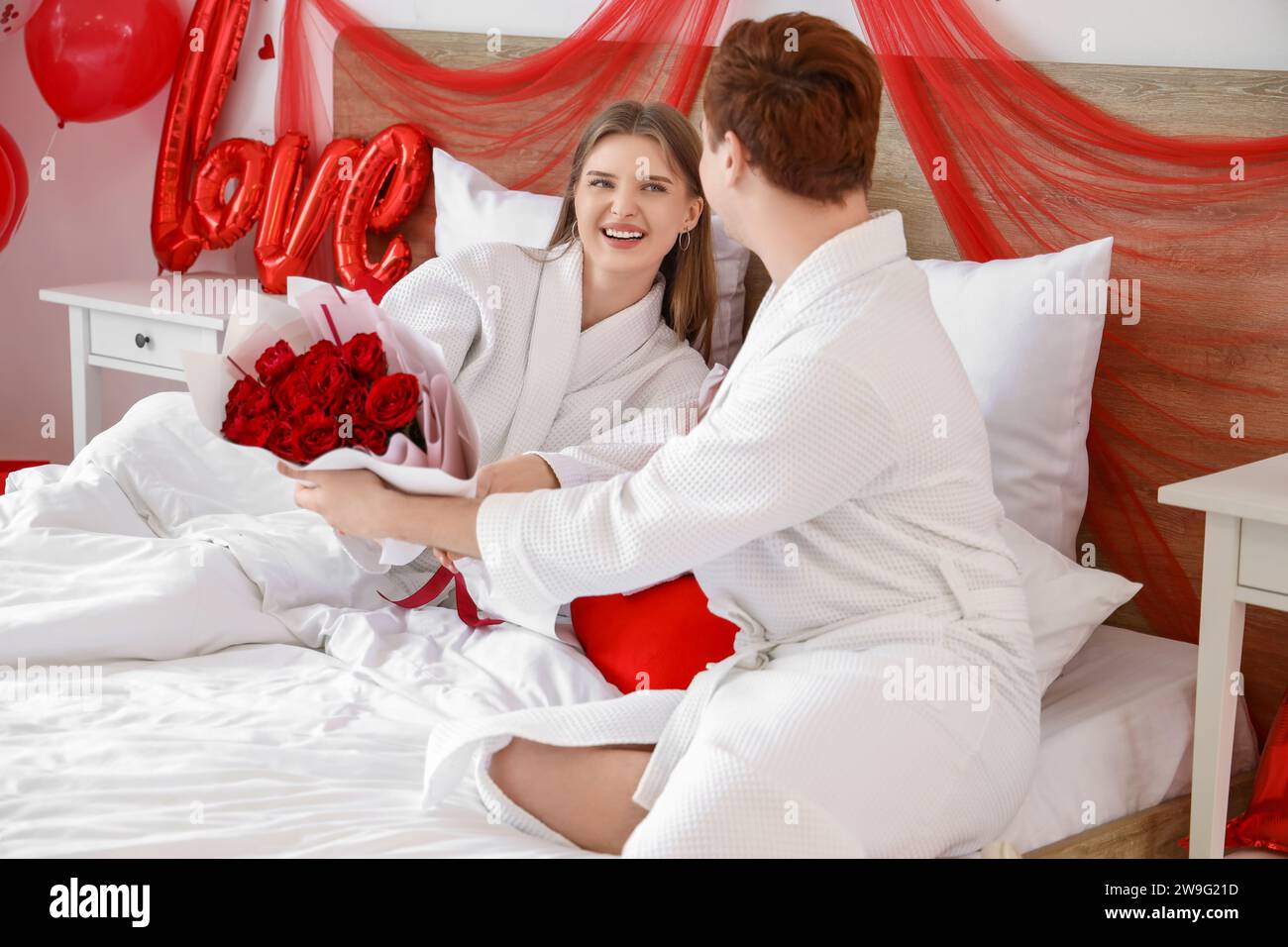 Young woman receiving roses from her boyfriend in bedroom on Valentine ...