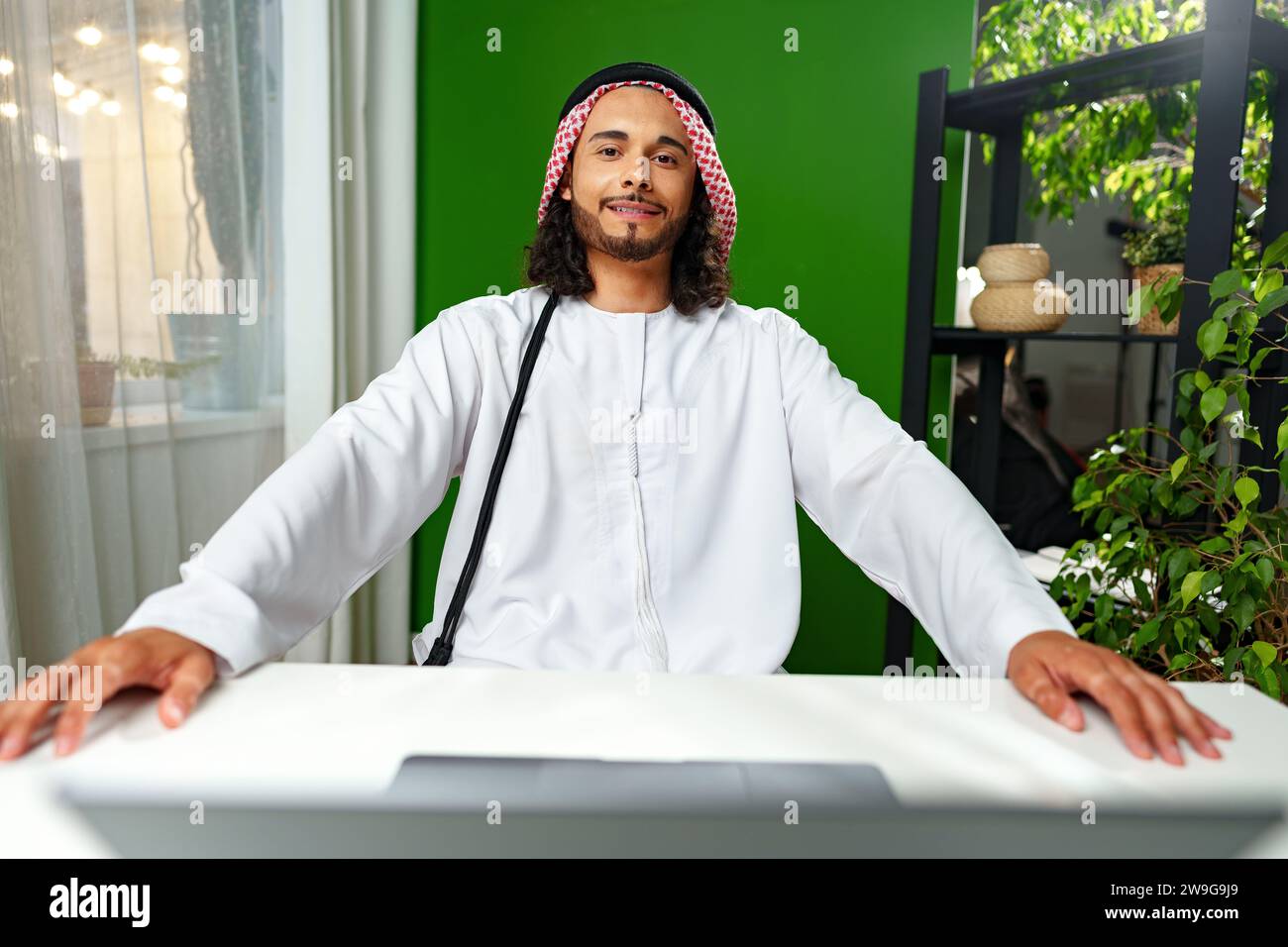 Young Arab man in traditional dress thobe working on computer in office ...