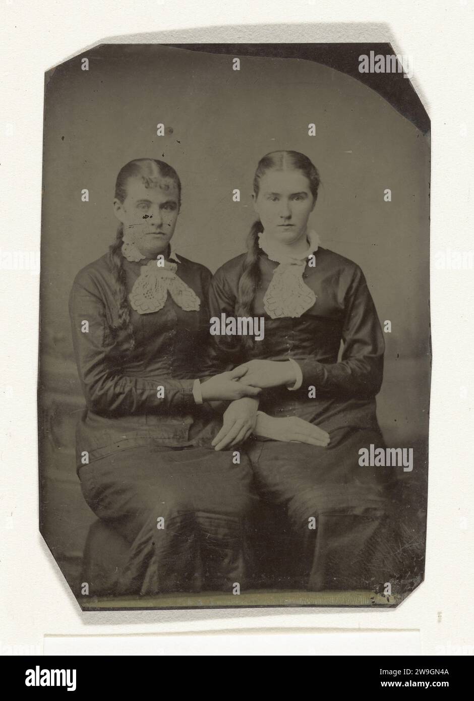 Portrait of two women, sitting next to each other and holding each ...