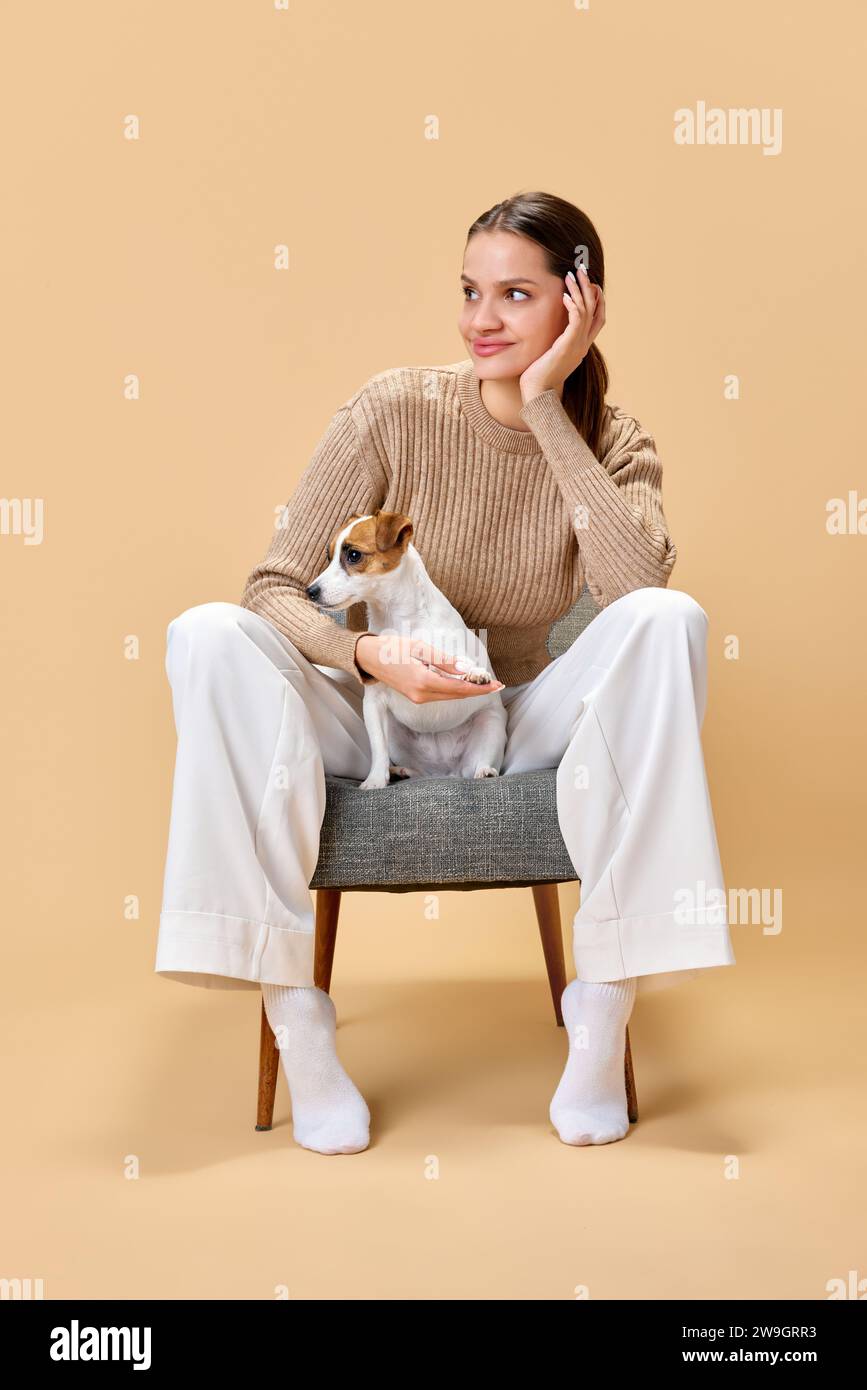 Young woman sitting on chair with her favorite pet, little playful dog ...