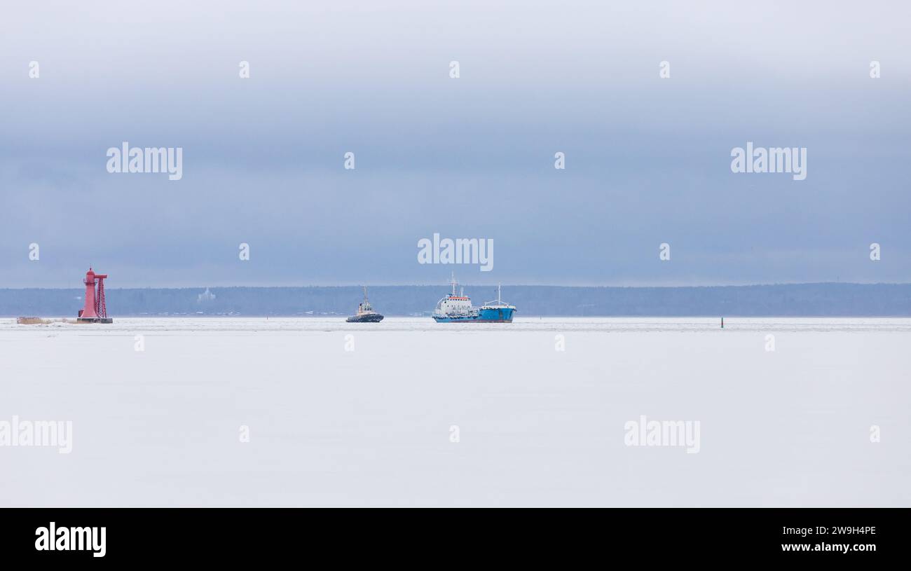 Cargo ship and a tugboat sail the channel on a winter day, ice ...