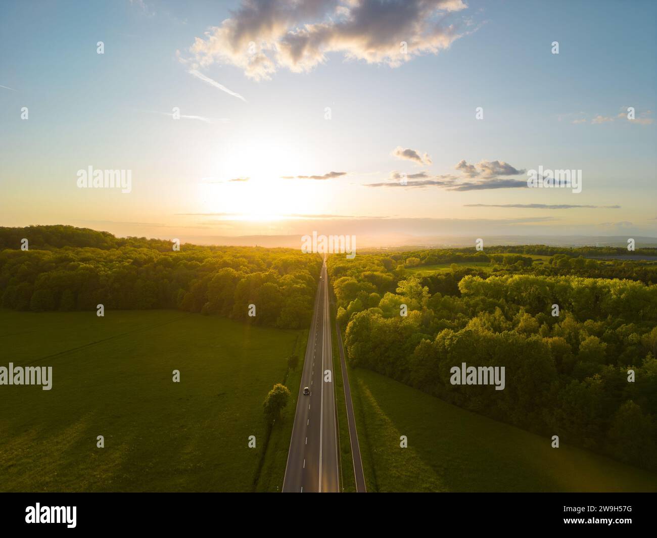 An aerial view of a straight road going through a forest at sunset in ...