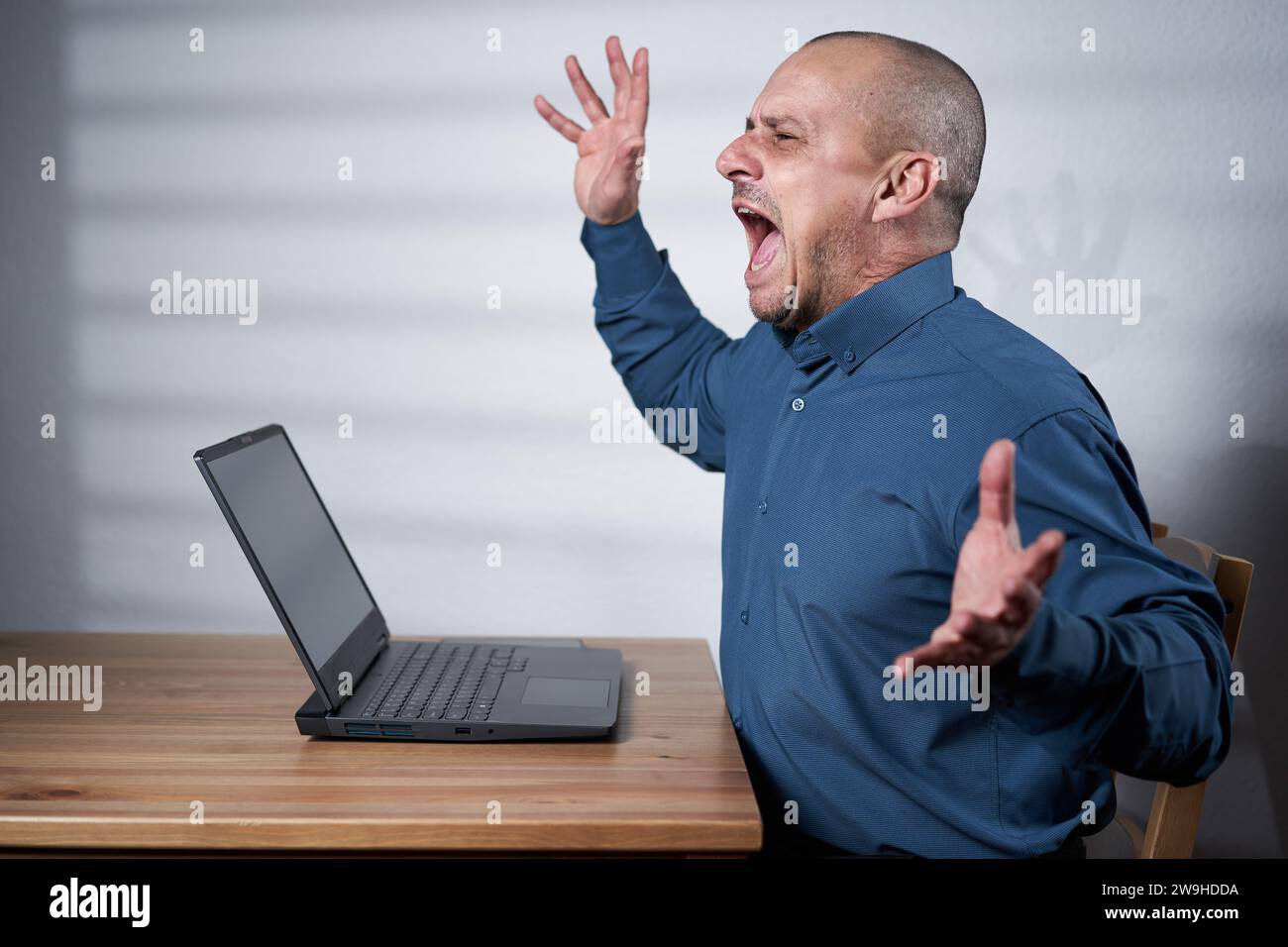 Mature business man sitting at his desk in front of his laptop, furious ...