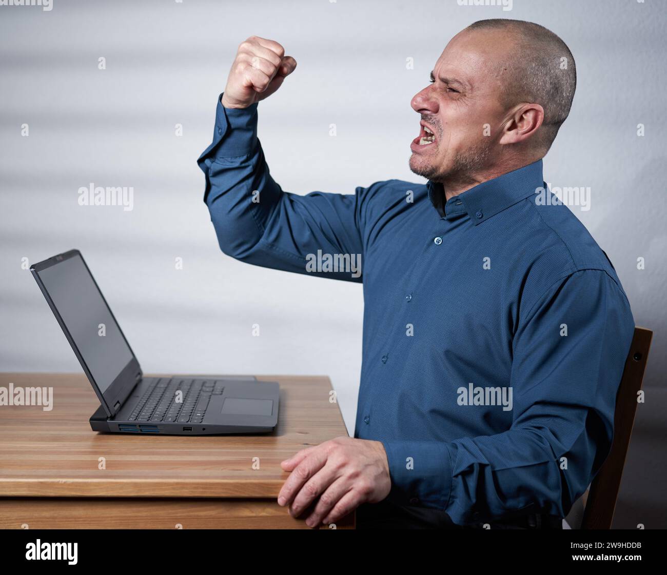 Mature business man sitting at his desk in front of his laptop, angry ...
