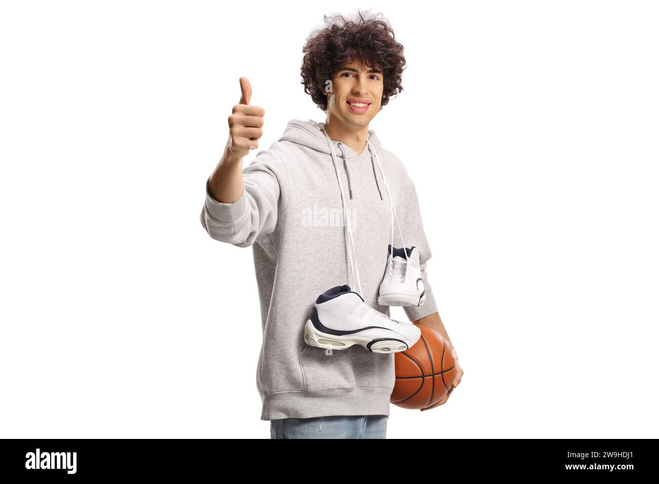 Smiling young man carrying basketball shoes and a ball and gesturing ...