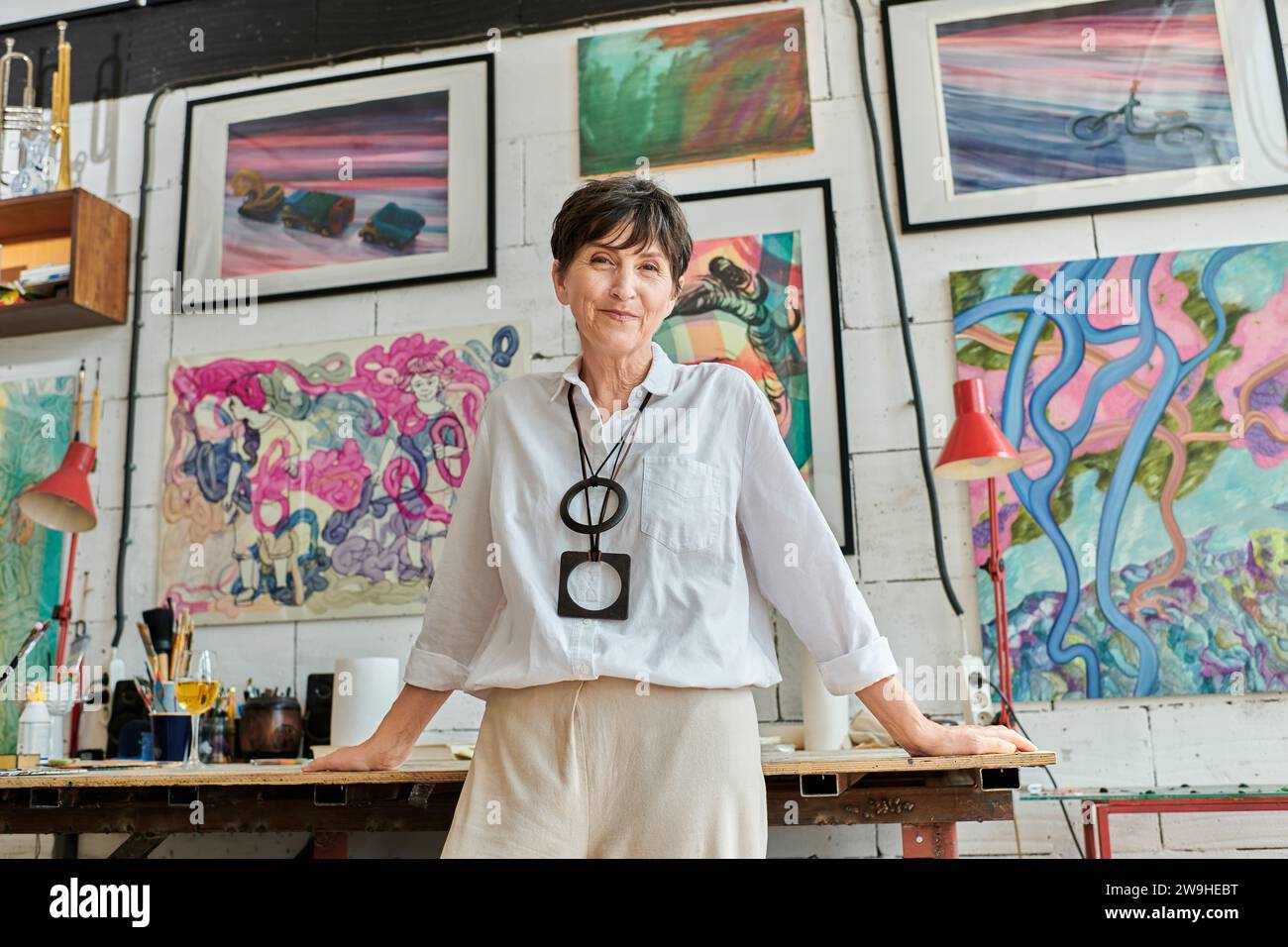 cheerful and stylish woman artist looking at camera in art studio with ...