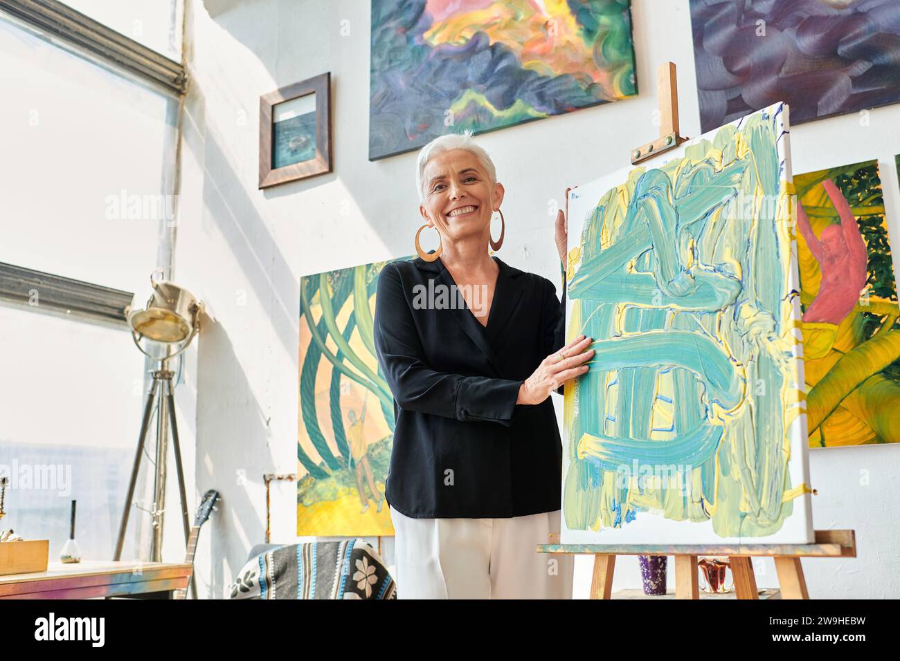 elegant and excited female artist smiling at camera near easel and ...