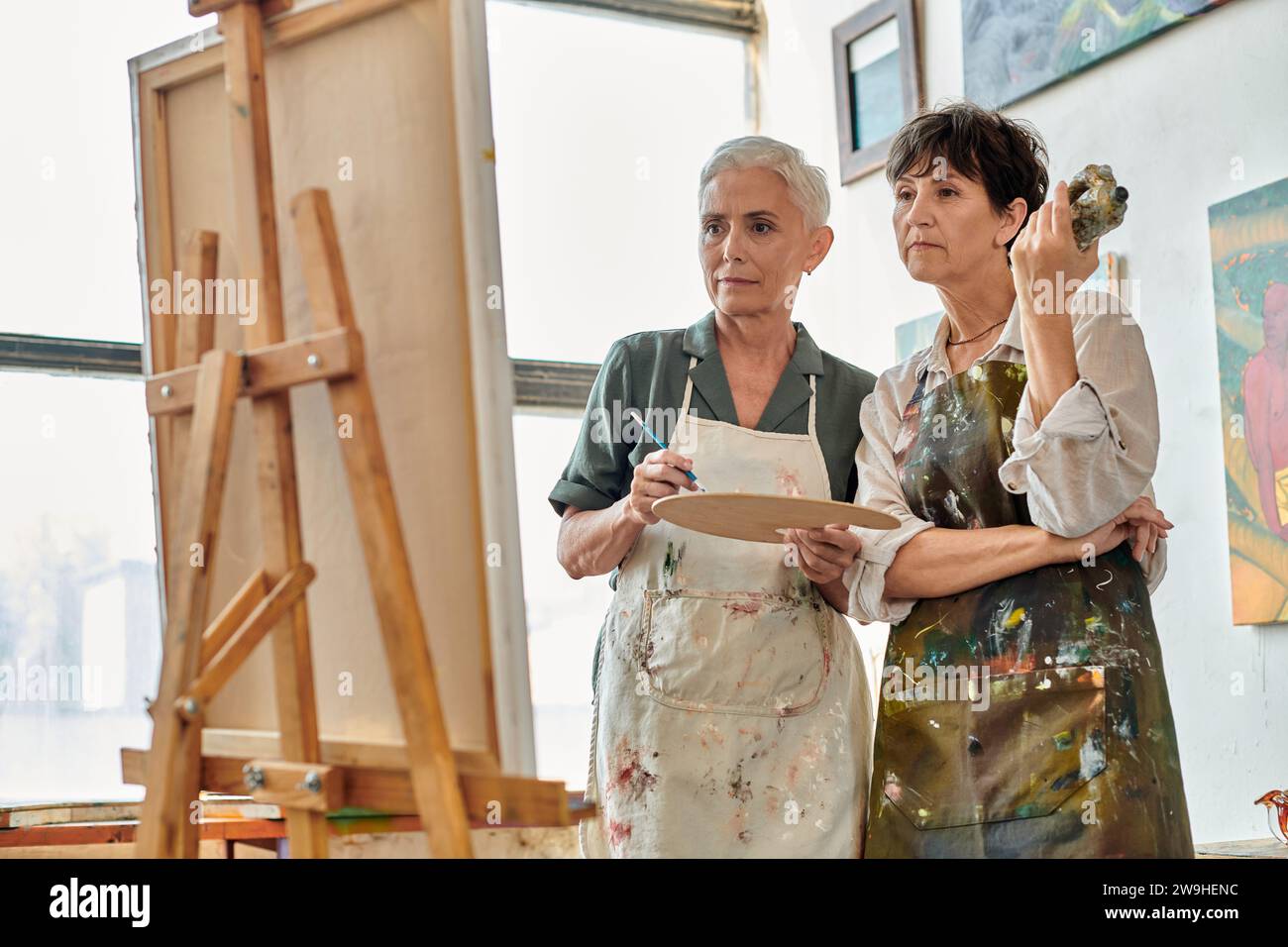 thoughtful and creative mature women looking at easel during painting ...