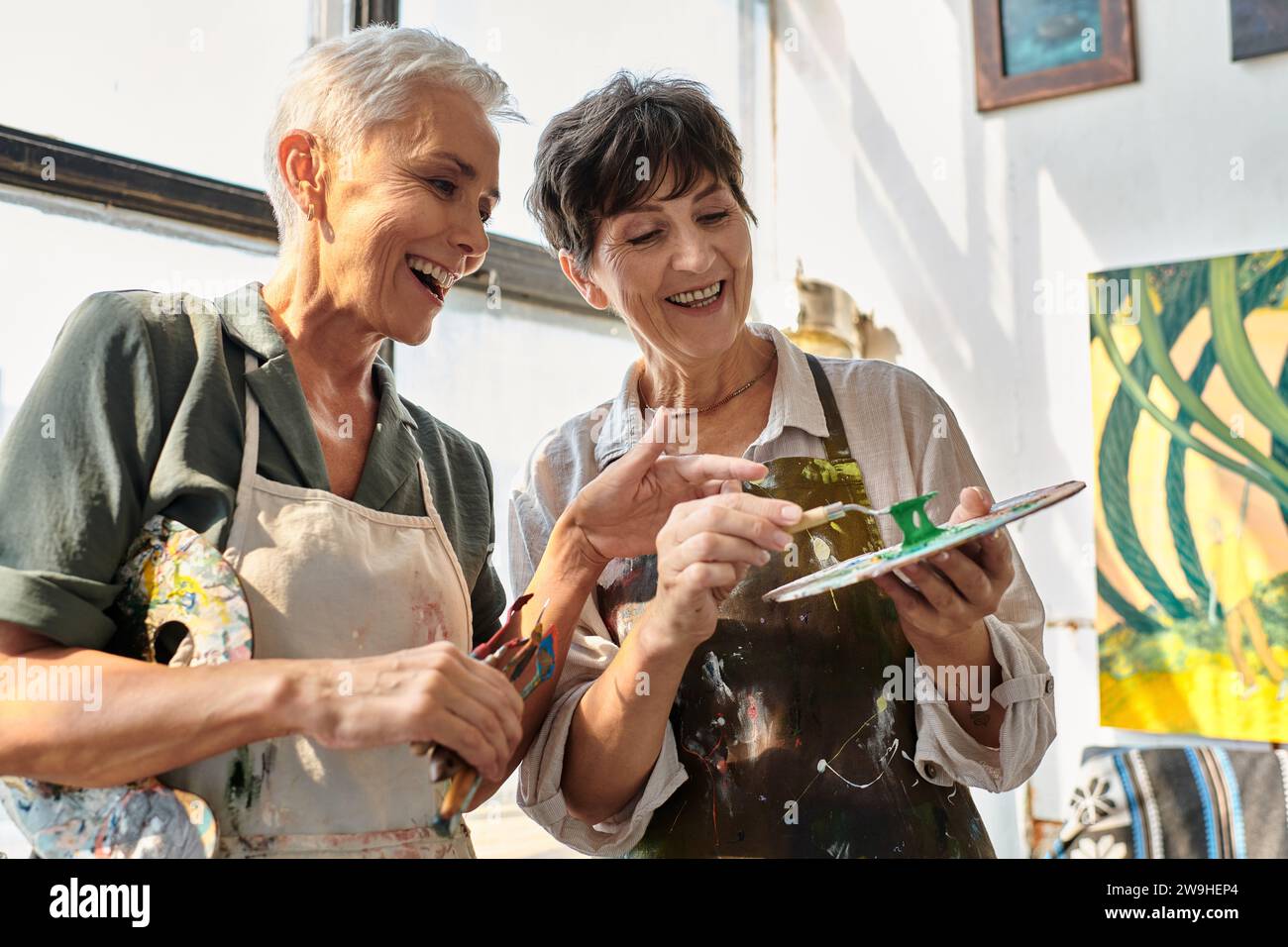 cheerful female artist helping mature woman mixing paints on palette ...