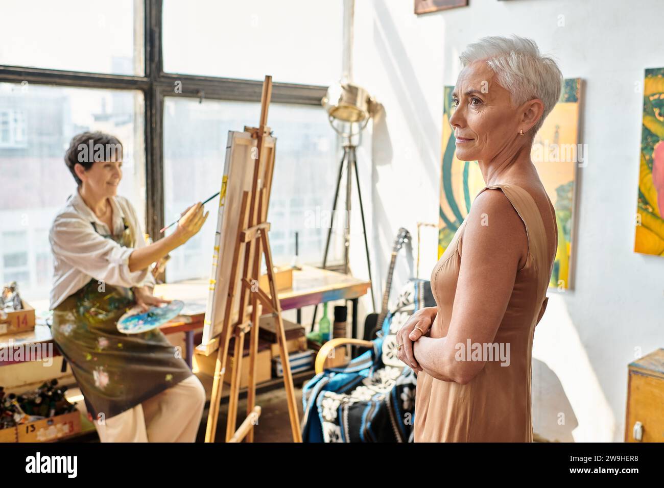 Elegant Middle Aged Model Posing Near Female Artist Painting In