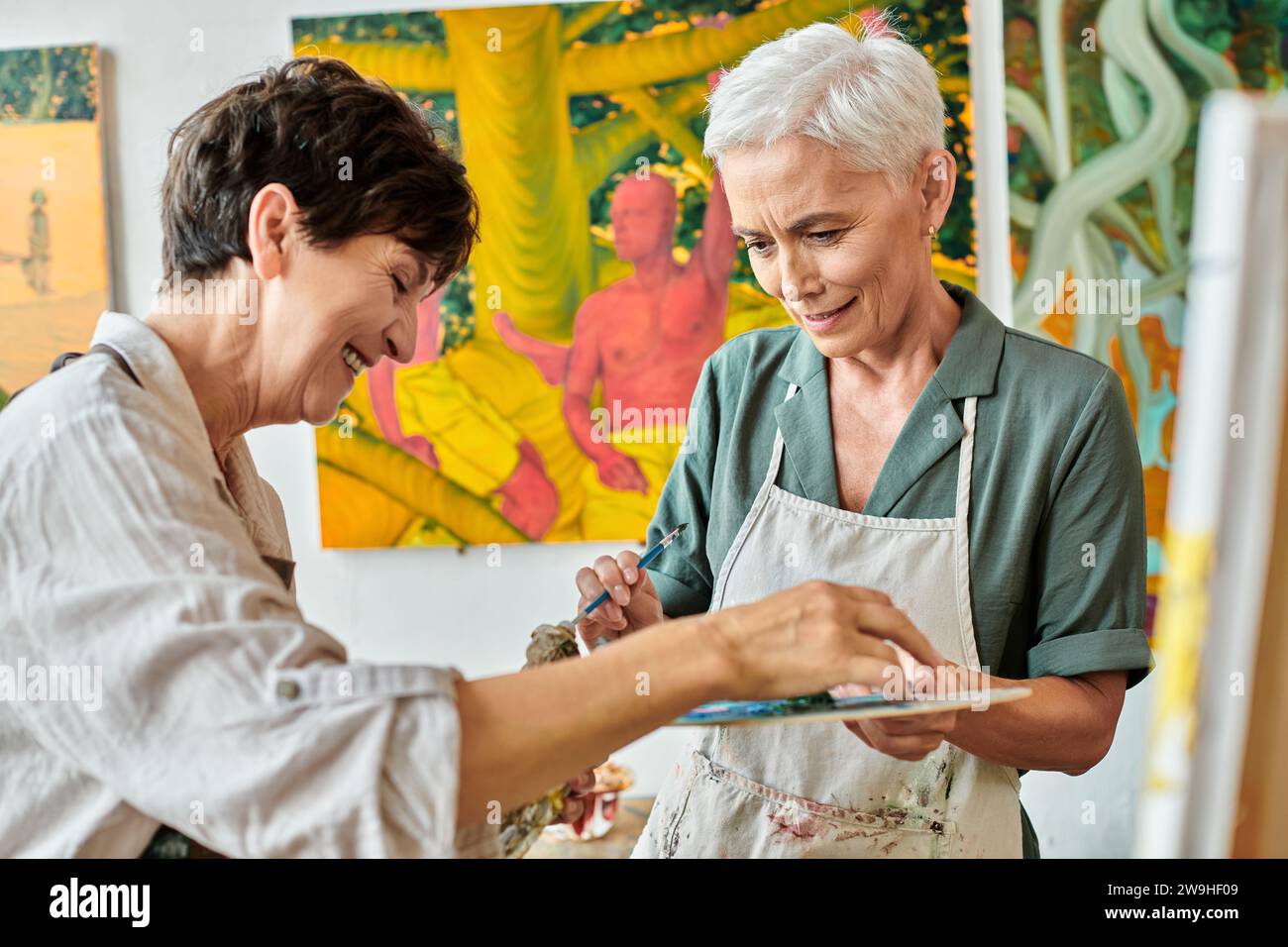 cheerful mature women mixing paints on color palette during painting ...