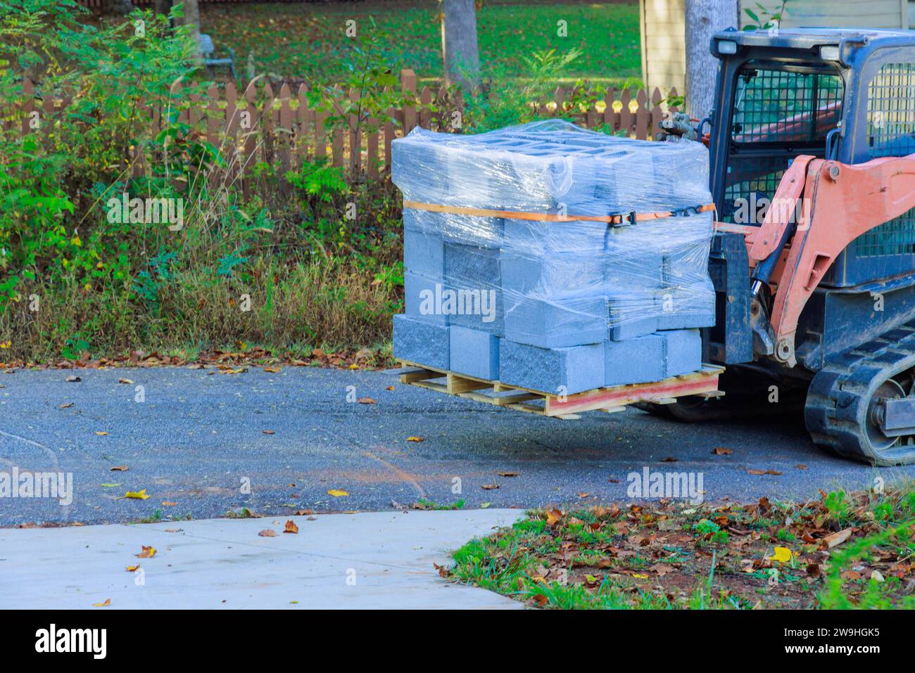Concrete blocks for retaining walls are lifted from pallets by worker operating small tractor ...