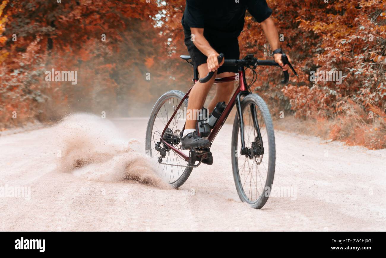 Cyclist on bike rides along the gravel road raising dust from the rear ...