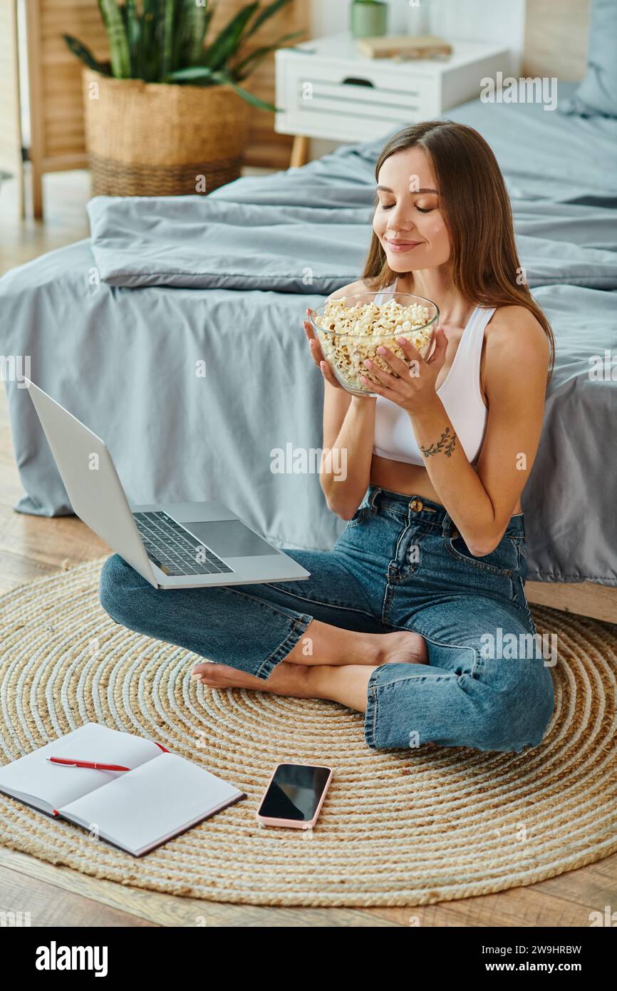 cheerful young woman in homewear with long hair with laptop on her legs ...